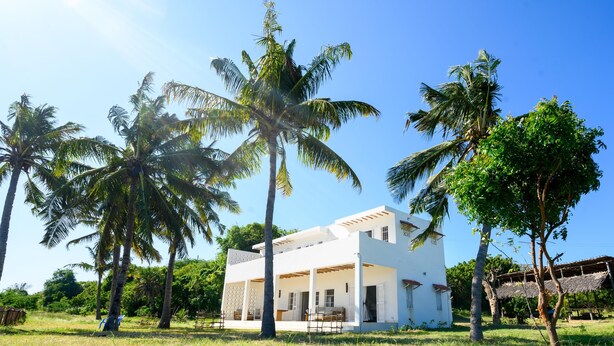 Um edifício branco de dois andares com área externa coberta, cercado por palmeiras.