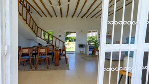 Ampla sala de estar com escada de madeira, conjunto de jantar e vista para o exterior.