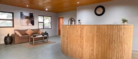 Um quarto amplo com teto de madeira, um balcão de recepção redondo em madeira, um sofá, uma mesa de centro e um relógio na parede.