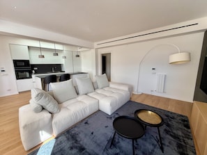 Uma sala de estar moderna com um sofá seccional, uma área de jantar e uma cozinha ao fundo.