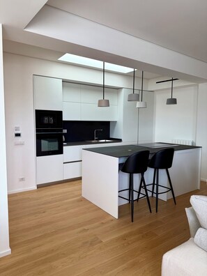 Cozinha moderna com ilha central, banquetas pretas e iluminação pendente.