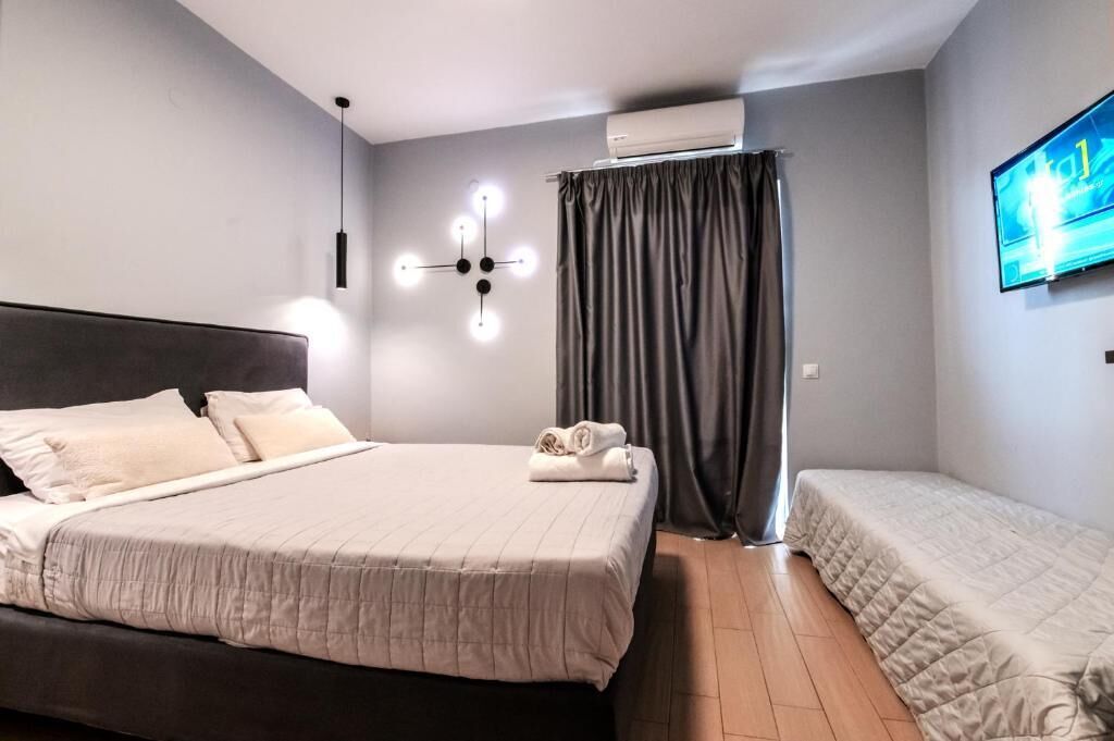 Quarto com cama, uma cama adicional, televisão, ar condicionado e luminária fixada na parede.