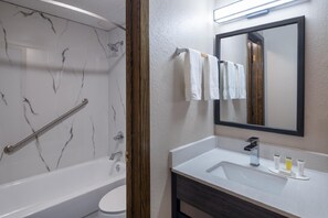 Uma casa de banho com parede de mármore, banheira, sanita, lavatório com espelho e um porta-toalhas.