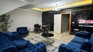 Uma sala de estar moderna com um sofá azul-escuro, uma mesa de jantar com cadeiras e uma TV de tela plana na parede.