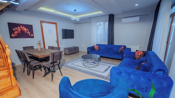 Uma sala de estar moderna com um sofá azul, uma mesa de jantar com cadeiras, uma mesa de centro e uma escada.