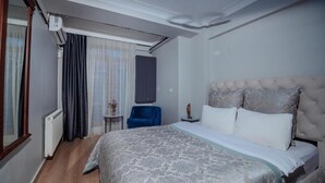 Quarto com cama, cadeira, mesa pequena e janela com cortinas.