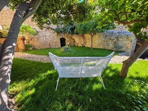 Uma cadeira de vime branca num jardim com um muro de pedra e uma porta pequena.