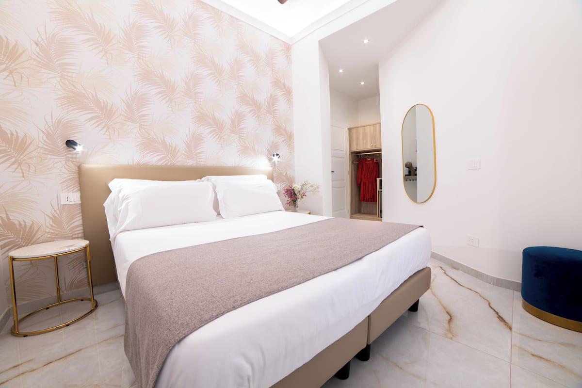 Quarto moderno com uma cama grande, mesa de cabeceira, espelho e guarda-roupa.