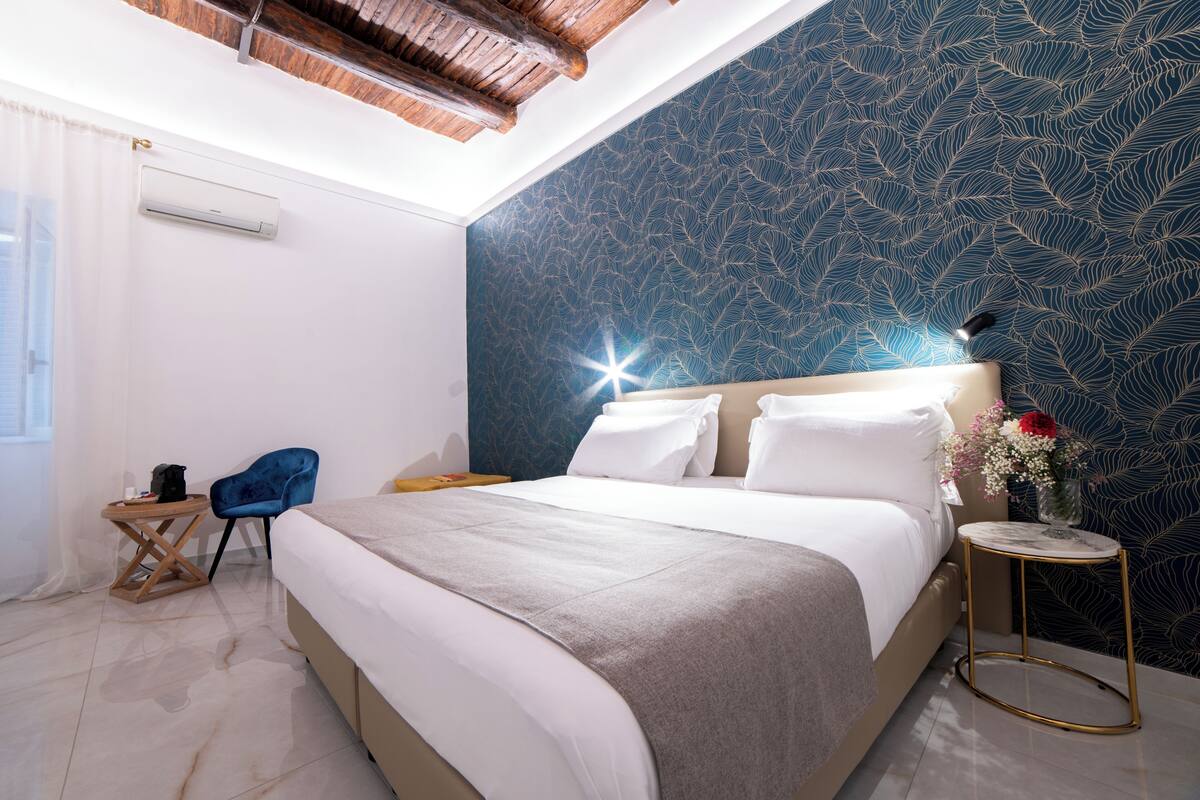 Um quarto com uma cama, uma cadeira azul, uma mesinha e um vaso decorativo.