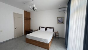 Um quarto com cama, guarda-roupa de madeira, mesa de cabeceira, luminária pendente e janela com cortinas.