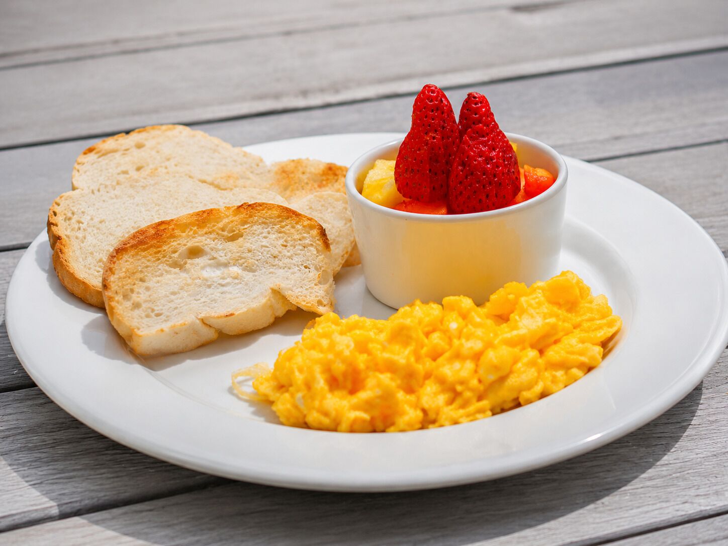 Um prato com ovos mexidos, torradas e uma cesta de frutas com morangos.
