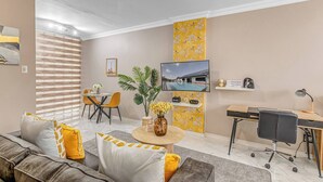Uma sala de estar moderna com sofá, mesa de centro, televisão e escrivaninha com cadeira.