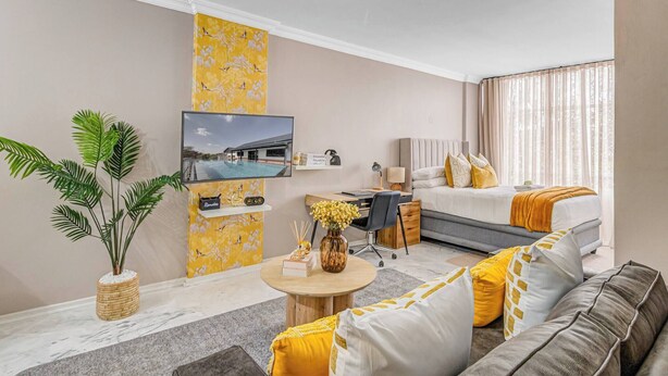 Uma sala de estar moderna com sofá, mesa de centro, TV, escrivaninha e cama.