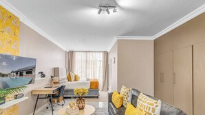 Uma sala de estar moderna com sofá, escrivaninha, televisão e uma janela grande com cortinas.