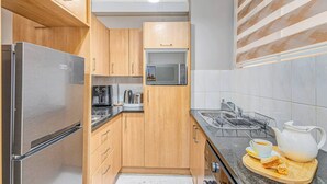 Cozinha moderna com armários de madeira, eletrodomésticos de aço inoxidável, micro-ondas, chaleira e espaço para café.