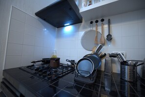 Uma cozinha com fogão a gás, panelas, frigideiras e diversos utensílios.