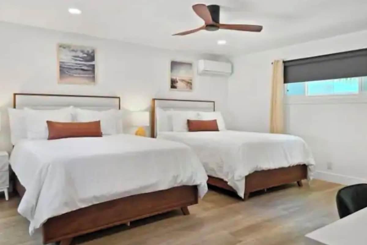Quarto de hotel com duas camas, ventilador no teto e obras de arte nas paredes.