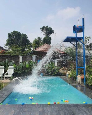 Piscina com fonte, cercada por vegetação e uma estrutura de telhado telhado.