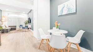 Uma sala de estar moderna com uma parede de destaque cinza, uma mesa de jantar redonda com cadeiras brancas e um sofá ao fundo.