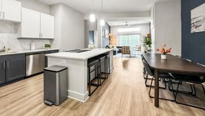 Uma cozinha moderna com uma ilha central, eletrodomésticos de aço inoxidável e uma área de refeições com mesa de madeira escura.