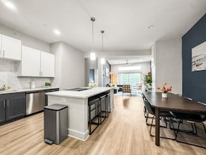 Uma cozinha moderna com uma ilha central, eletrodomésticos de aço inoxidável e uma área de refeições com mesa de madeira escura.
