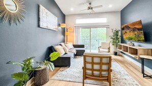 Uma sala de estar moderna com sofá, uma cadeira de madeira, TV e ventilador de teto.