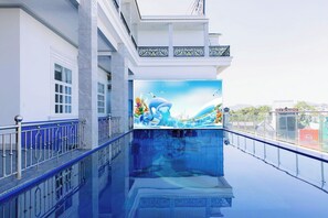 Piscina com um mural, varanda com guarda-corpo e fachada de edifício.