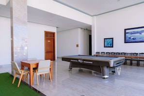 Uma mesa de bilhar numa sala com piso de mármore, porta de madeira e um quadro na parede.