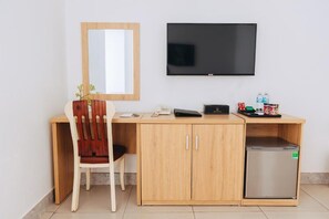 Quarto de hotel com escrivaninha de madeira, uma cadeira, televisão, frigorífico e espelho.