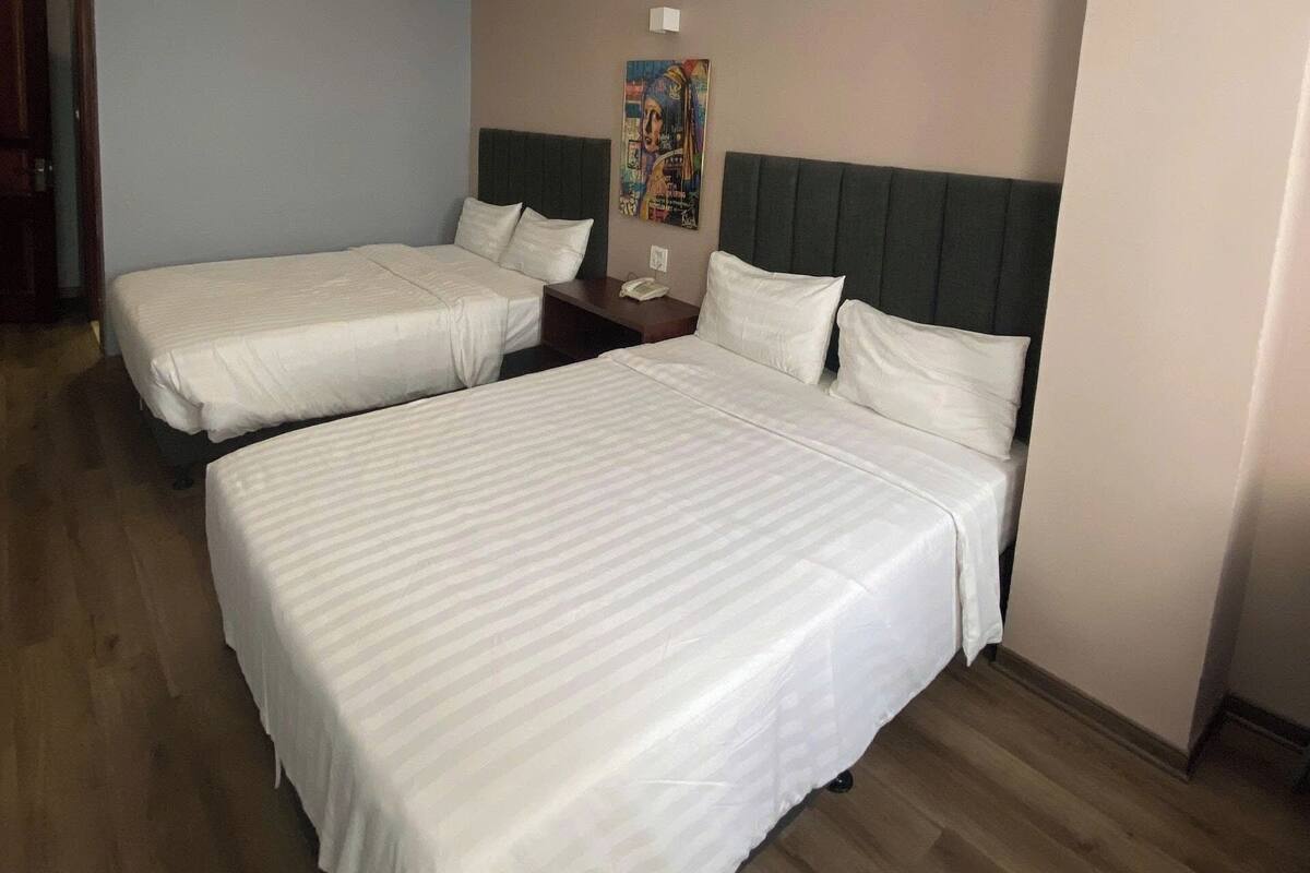 Quarto de hotel com duas camas, mesa de cabeceira, telefone e um pôster na parede.