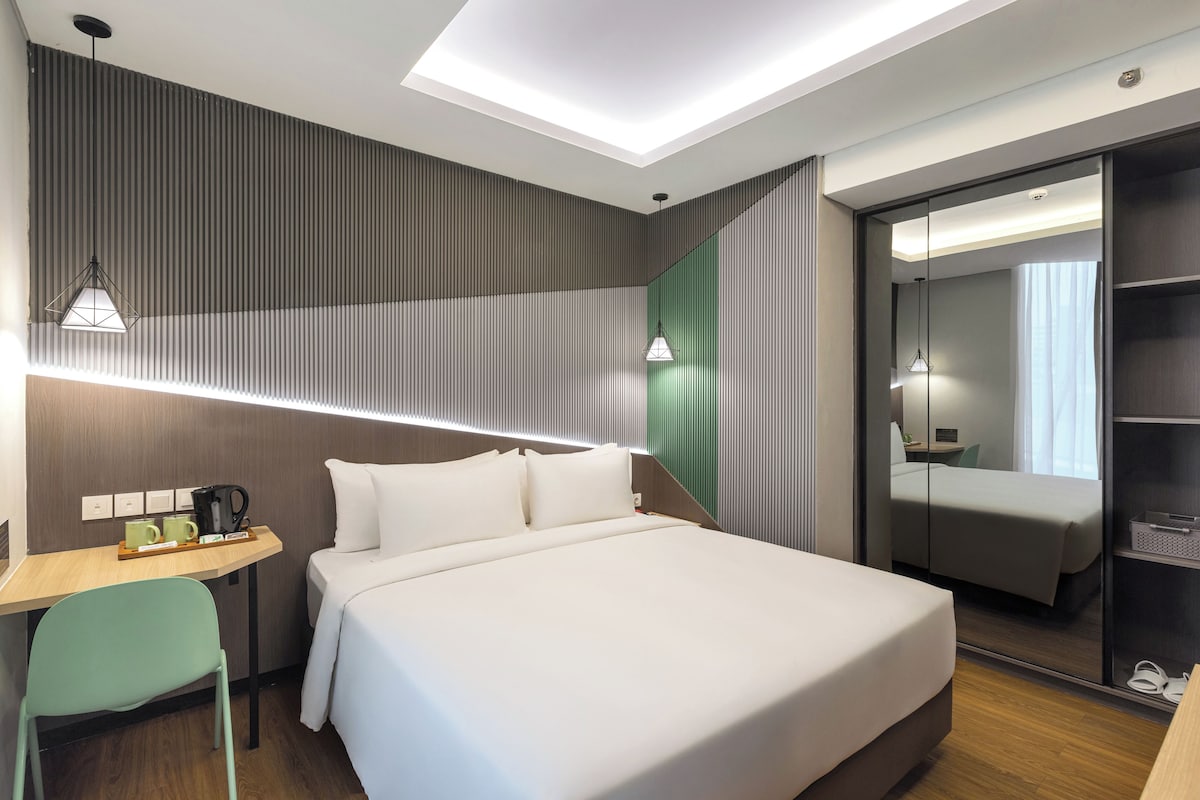 Quarto de hotel moderno com cama, escrivaninha, cadeira e guarda-roupa.