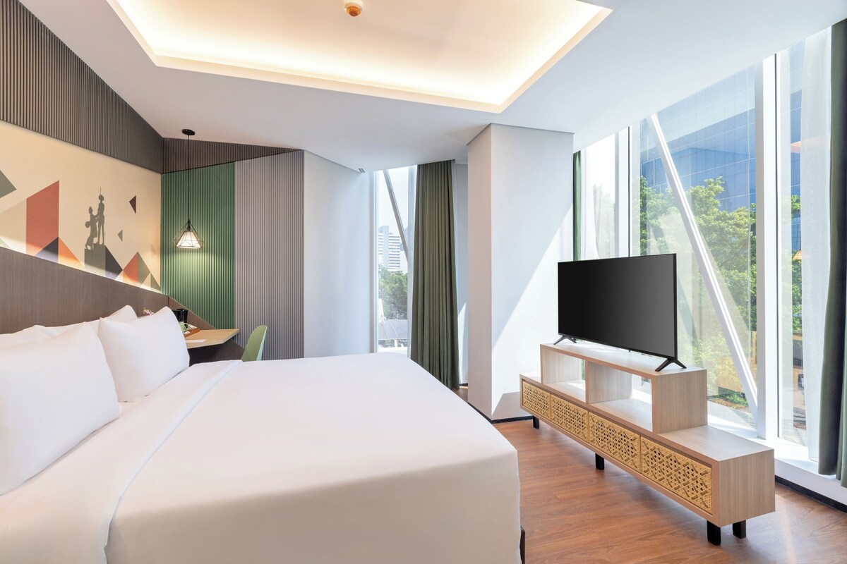 Quarto de hotel moderno com uma cama grande, televisão de tela plana e vista da cidade por grandes janelas.