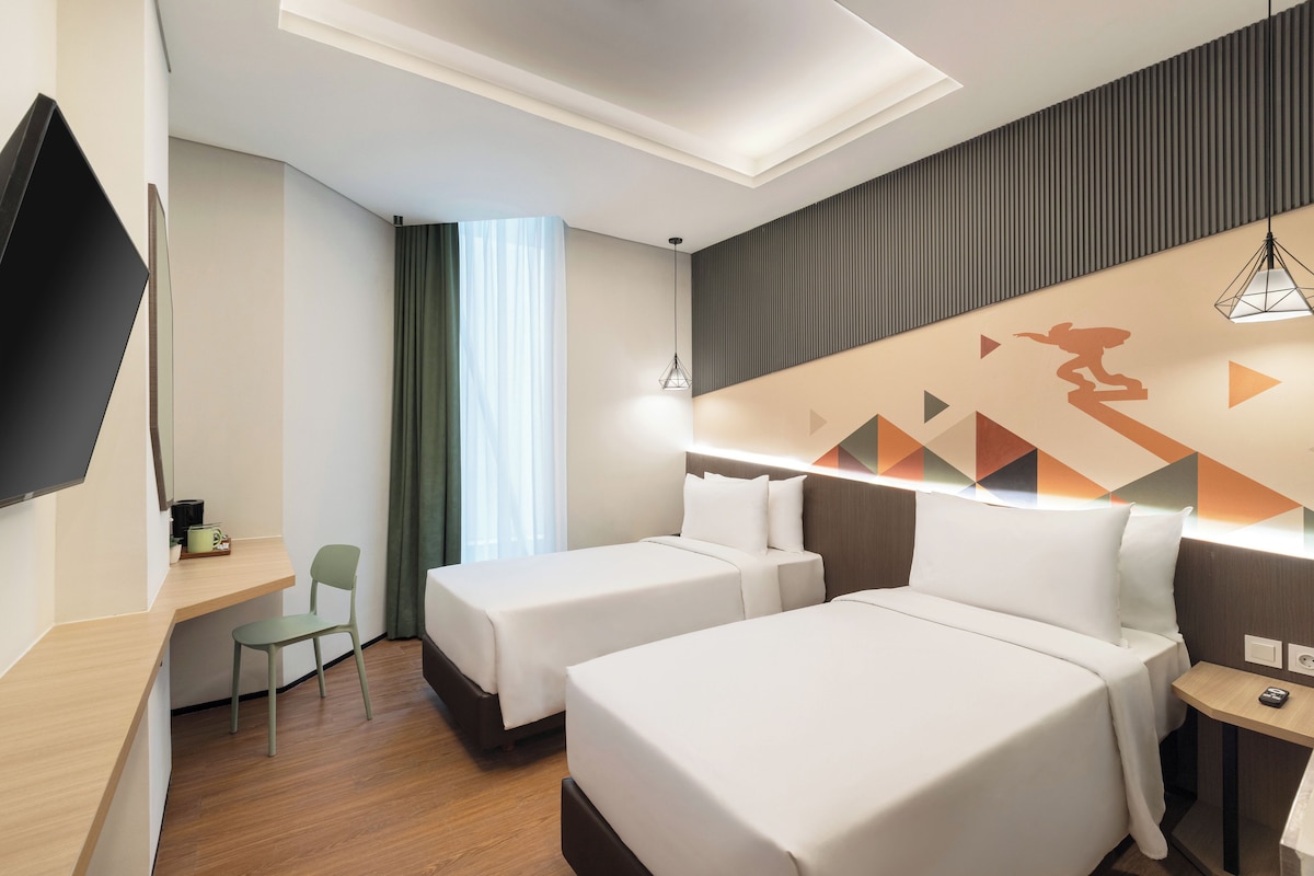 Quarto de hotel com duas camas, uma escrivaninha, uma cadeira, uma televisão e parede com padrões geométricos.