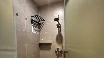 Um pequeno banheiro revestido com azulejos, com chuveiro, mangueira e porta-toalhas na parede.