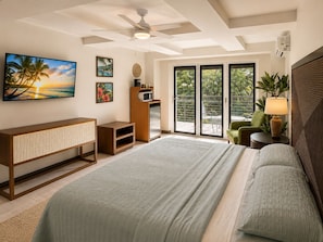 Quarto com cama, televisão, ventoinha no teto, secretária, cadeira e varanda com vista para árvores.