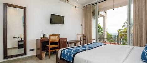 Quarto de hotel com cama, escrivaninha, cadeira, televisão e varanda com vista.