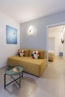 Uma sala de estar moderna com um sofá, uma mesa de centro de vidro, um quadro na parede e uma porta que dá para outro cômodo.