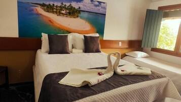 Quarto de hotel com uma cama, um quadro de uma praia, uma janela e uma mesa de cabeceira.