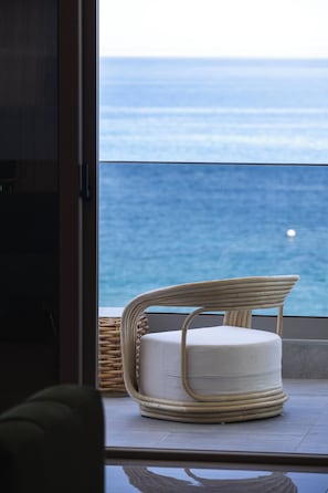 Uma cadeira branca estofada com estrutura de fibra em uma varanda com vista para o oceano.