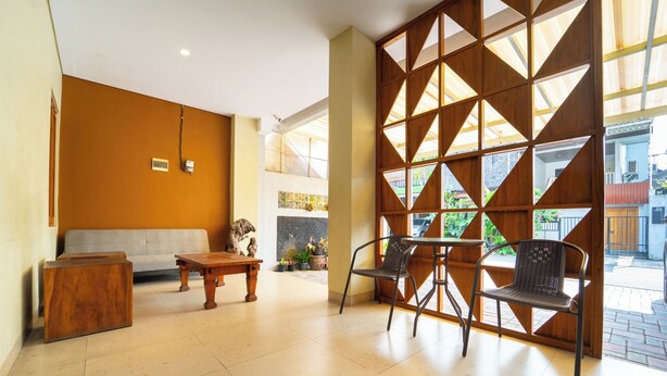 Uma área de recepção com sofá, mesa de madeira, cadeiras e uma parede decorativa com padrões geométricos.