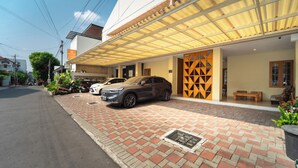 Um edifício com área de estacionamento coberta, dois carros estacionados e um caminho de tijolos até a entrada.
