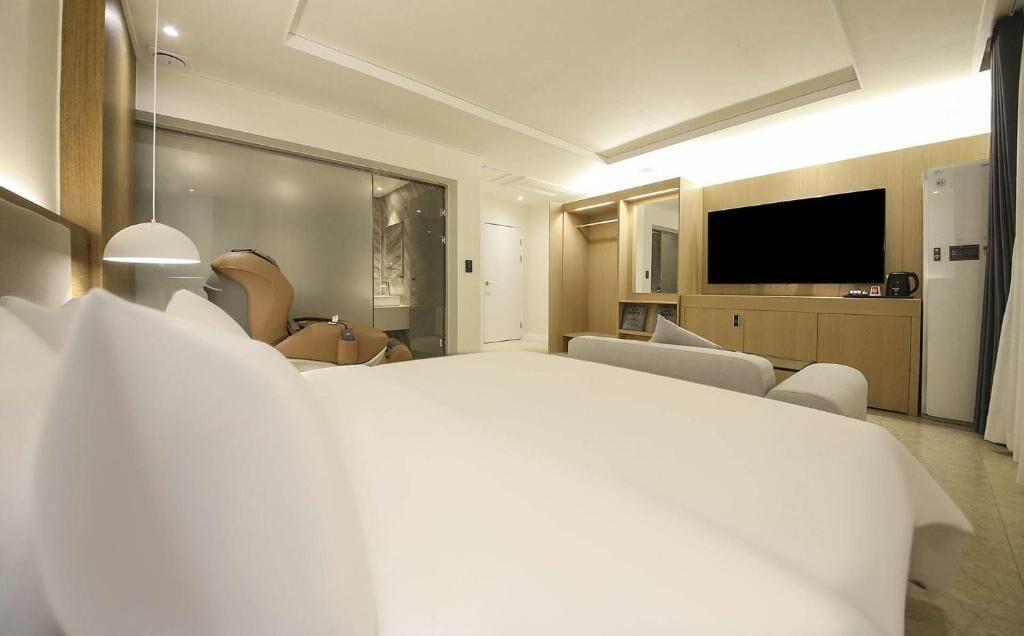 Quarto de hotel moderno com uma cama grande, área de estar, televisão e minibar.