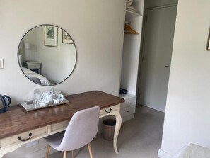 Quarto com escrivaninha de madeira, espelho redondo, cadeira, mesa de cabeceira e guarda-roupa.