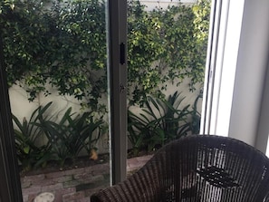 Uma cadeira de vime num quarto com porta de vidro que dá para um jardim com várias plantas.