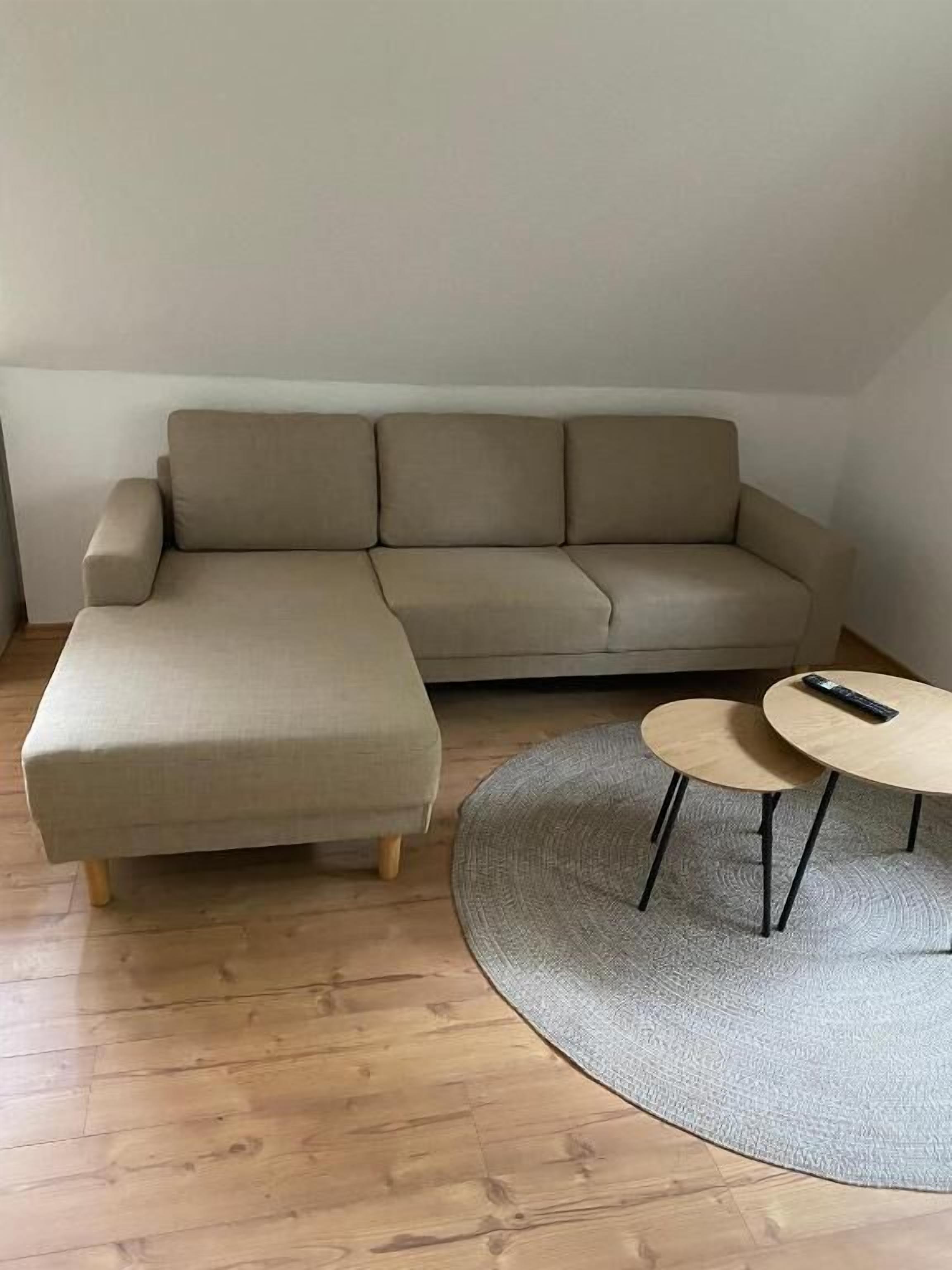 Uma sala de estar com sofá, um banquinho, duas mesinhas e um tapete redondo.