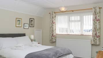 Um quarto com cama, radiador, janela com cortinas e luminária no teto.