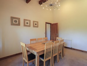Uma sala de jantar com mesa e cadeiras de madeira, um candelabro e quadros nas paredes.