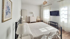 Quarto com cama, escrivaninha, cadeira, penteadeira, televisão e um quadro na parede.
