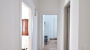 Um corredor com piso de madeira, paredes brancas e portas que dão acesso a outros cômodos.