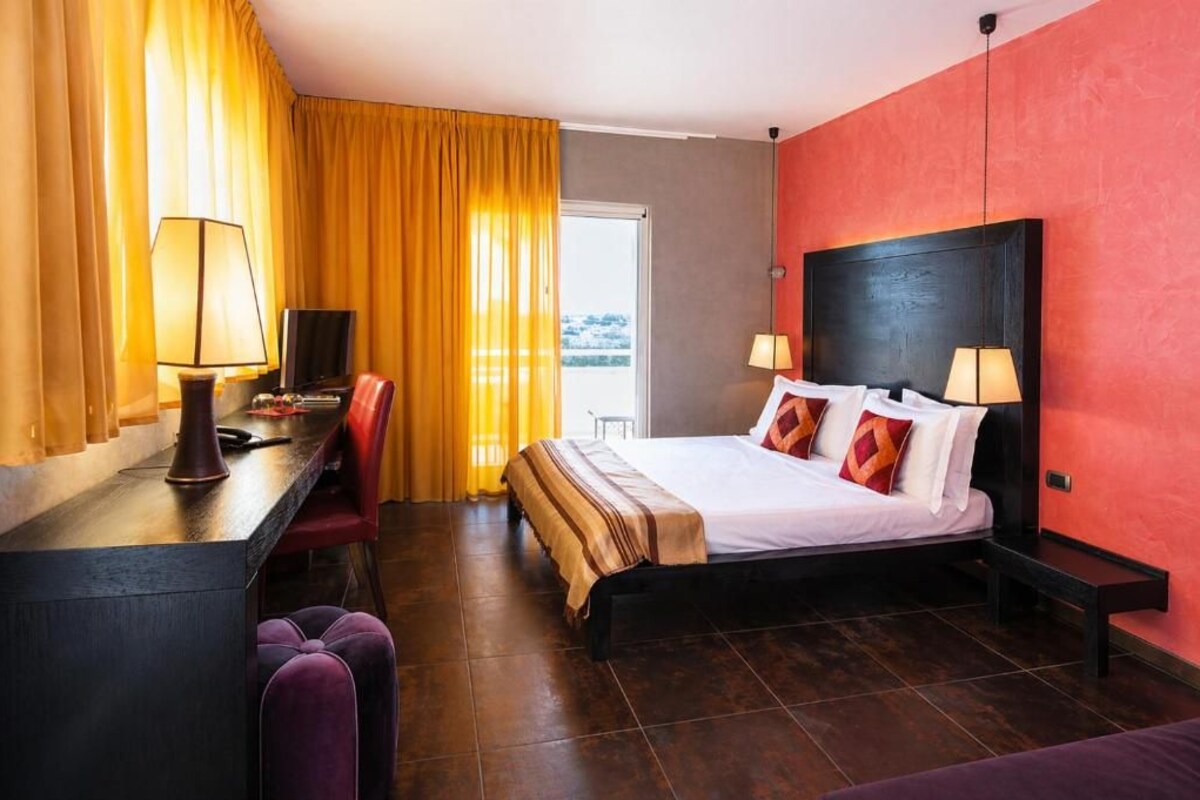 Quarto de hotel com cama, escrivaninha, cadeira e vista para o exterior.